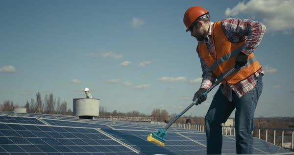 Medium shot of technician cleaning solar panels on flat roof while ...