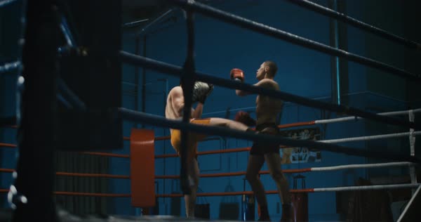 Handheld shot of two shirtless men in boxing gloves fighting and ...