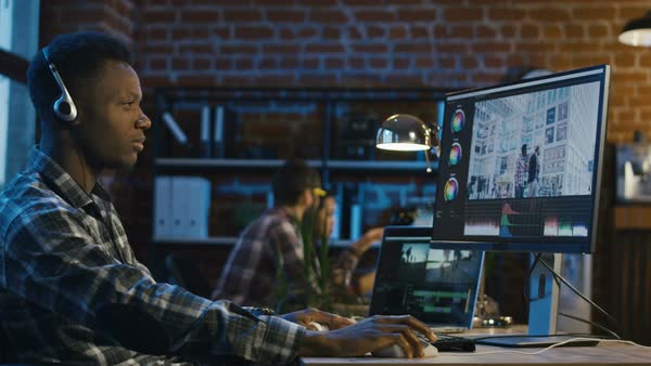 Side view of black man in headphones working on computer and editing ...