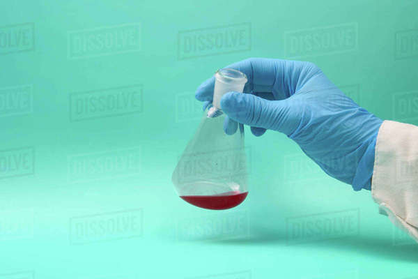 Unrecognisable hand shaking an Erlenmeyer flask with a red chemical ...