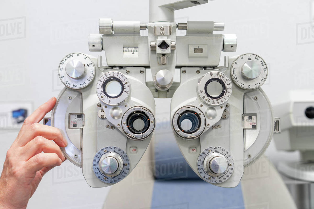 A hand adjusts the lenses on a phoropter, an instrument used by eye ...
