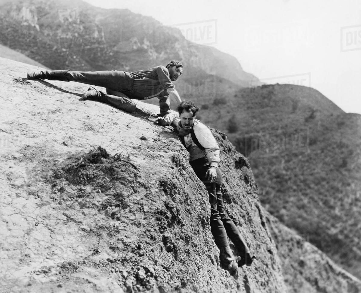 Man helping another man from falling down a cliff - Royalty-free Stock ...