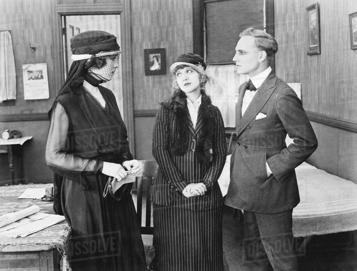 Three people standing together in a room talking with each other ...