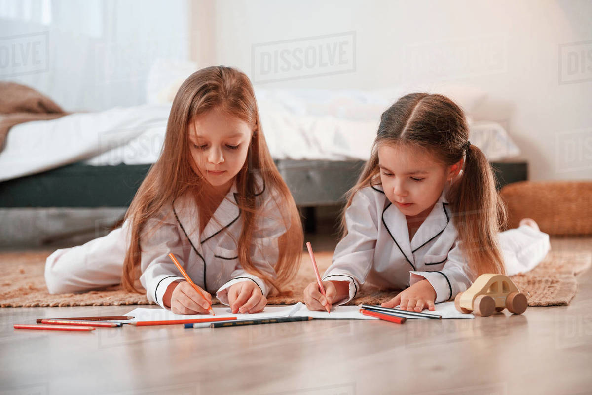 Two little girls are lying down on the ground and drawing together in ...