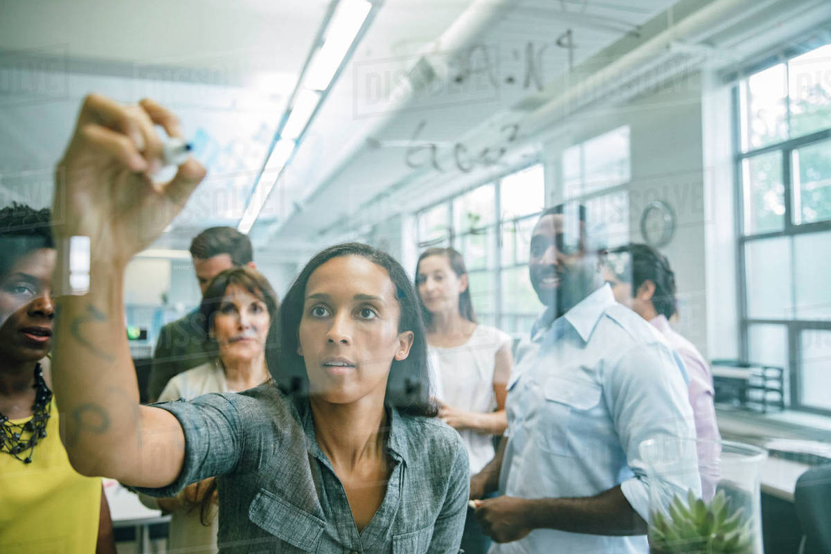 Woman writing on a glass wall during an office meeting - Royalty-free ...
