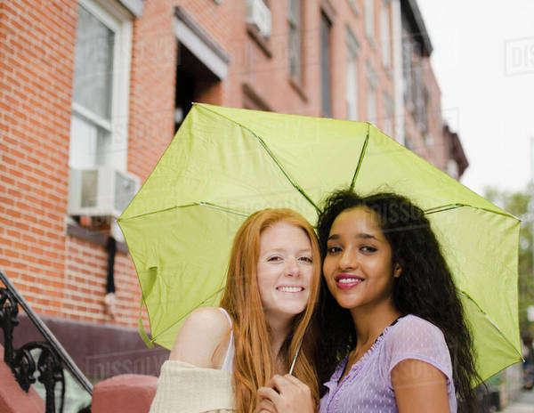 Friends sharing umbrella outdoors - Stock Photo - Dissolve