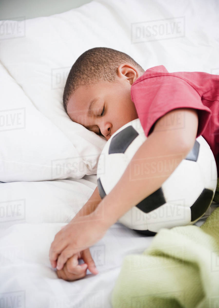 African American boy sleeping with soccer ball - Stock Photo - Dissolve