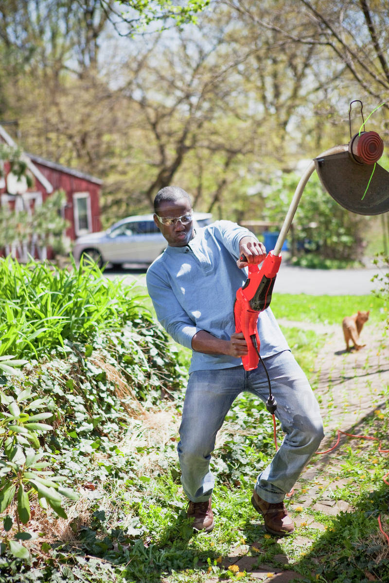 Black man struggling with weed trimmer - Stock Photo - Dissolve