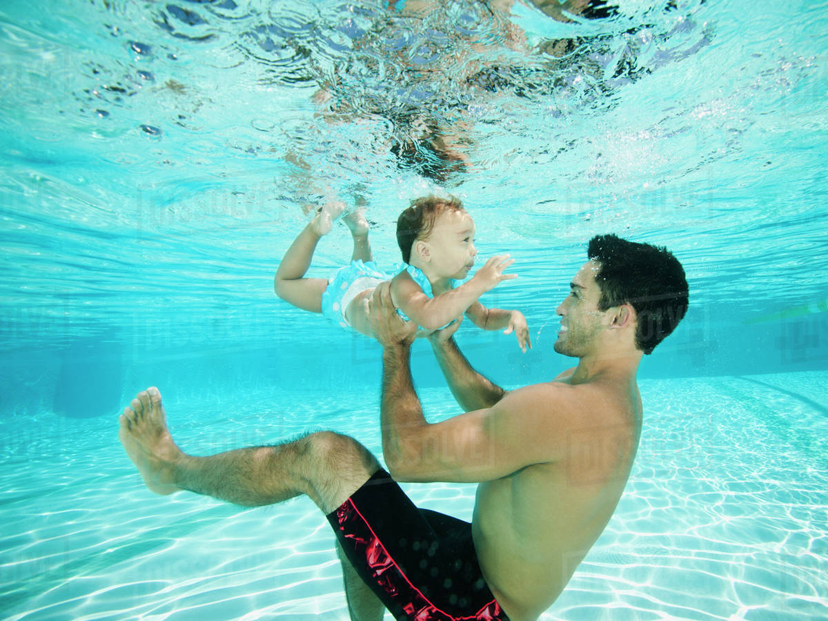 Father swimming underwater with daughter in swimming pool - Stock Photo - Dissolve