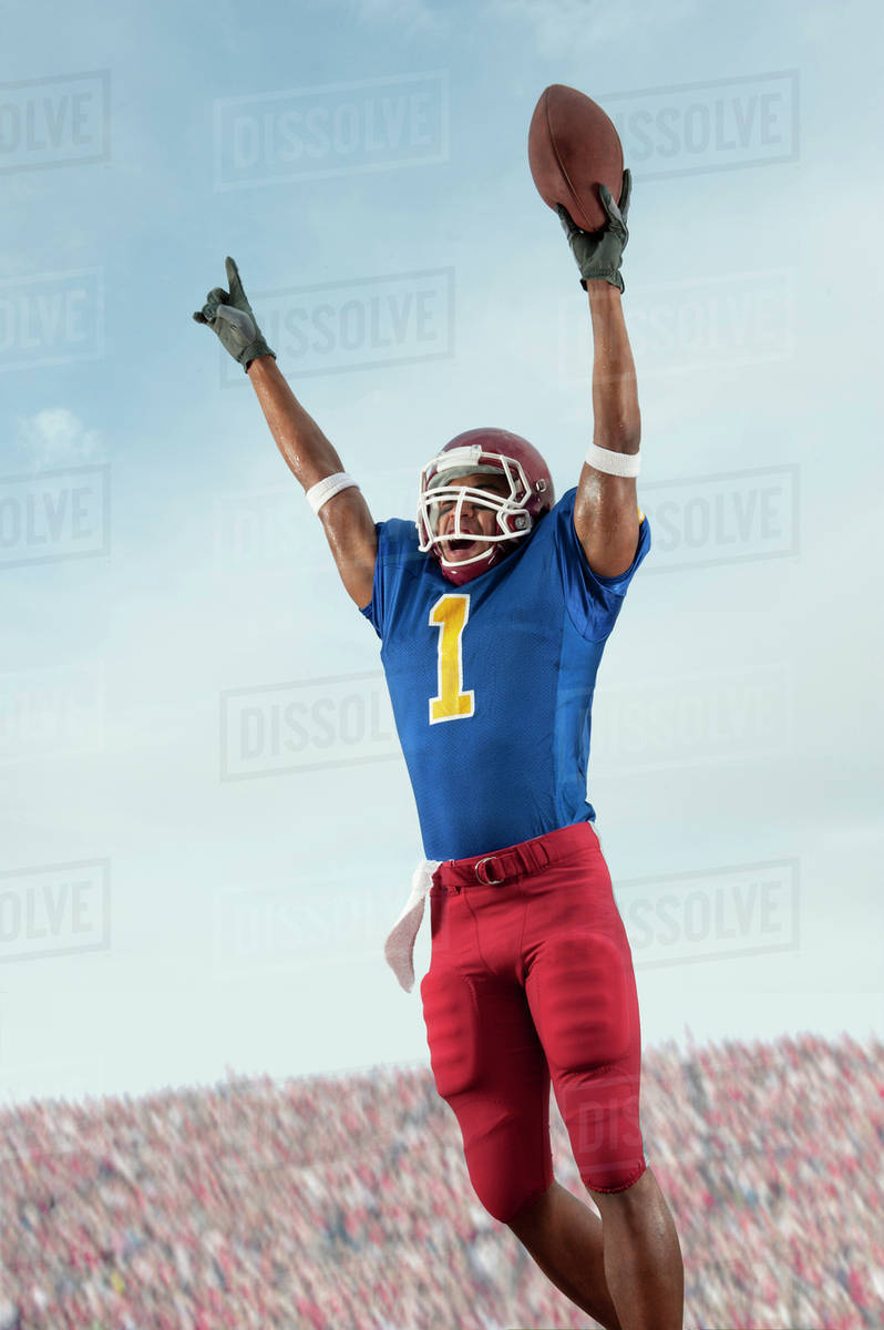 Mixed race football player with arms raised holding football - Stock ...