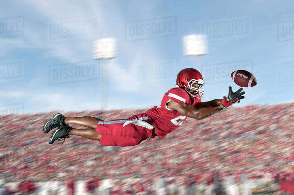 African American football player jumping in mid-air catching football ...