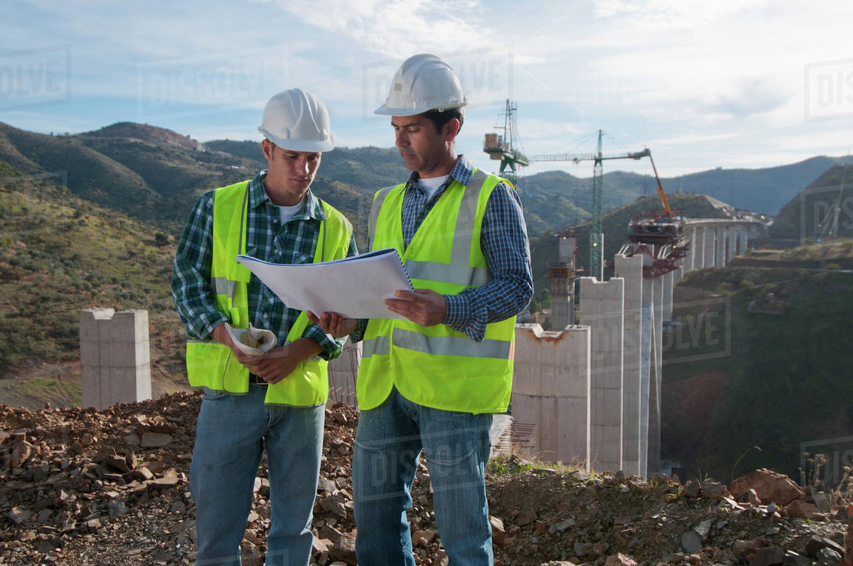 Construction workers looking at blueprint at construction site ...