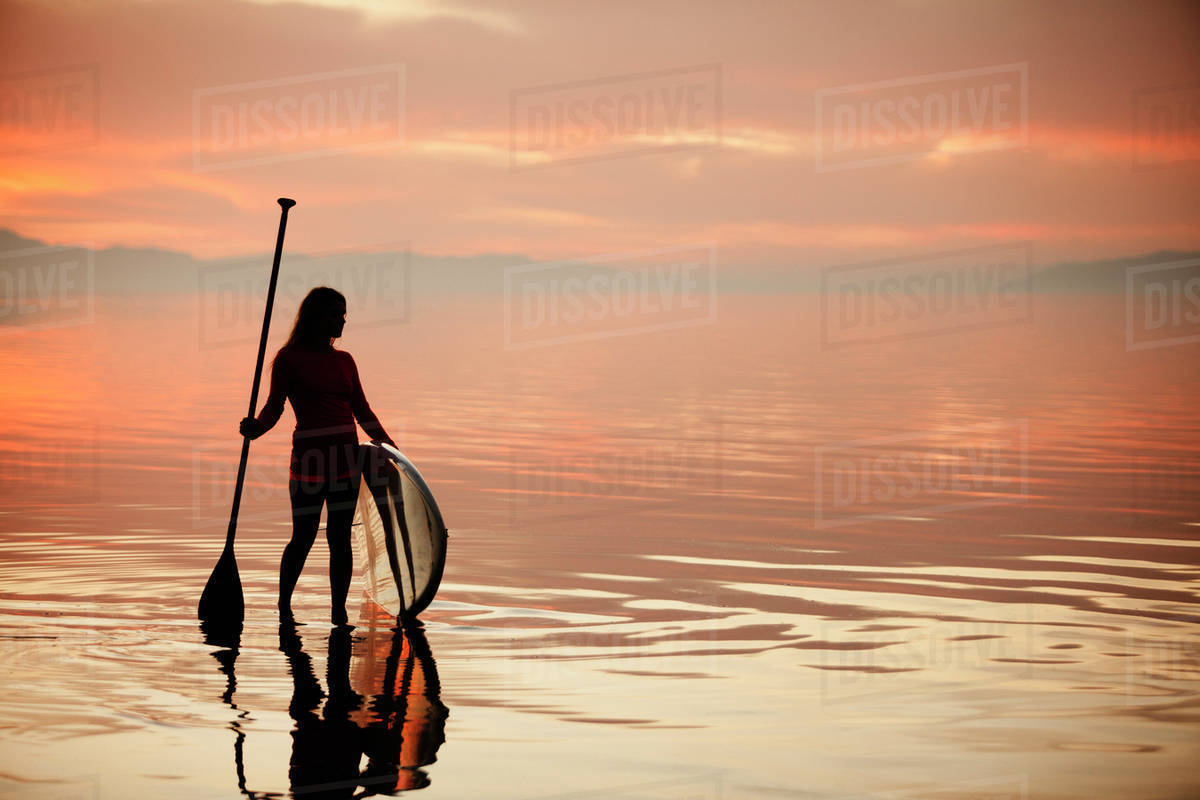 Caucasian woman standing with paddle board at sunset - Stock Photo ...