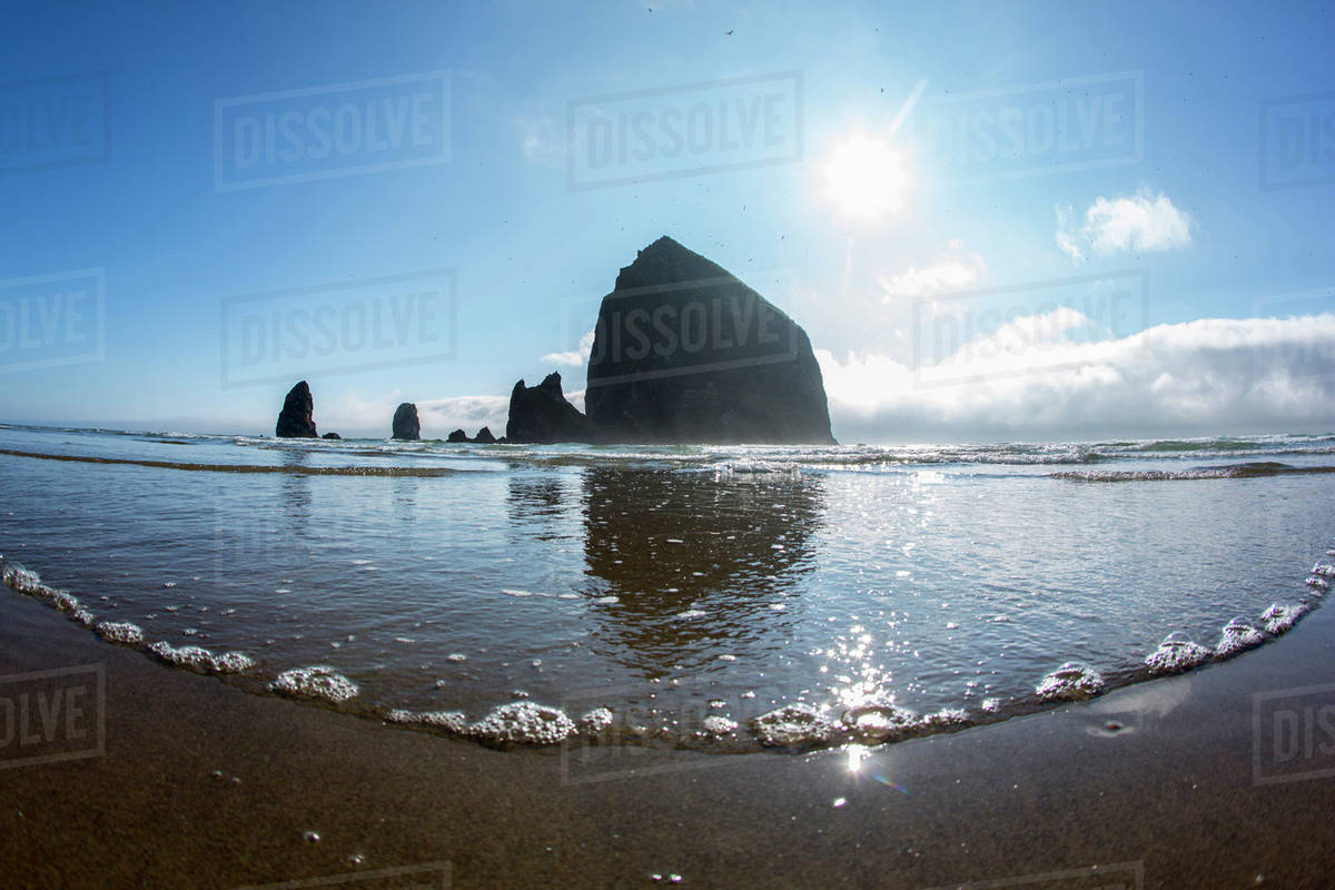 Low angle view of Haystack Rock reflecting in ocean waves, Cannon Beach ...