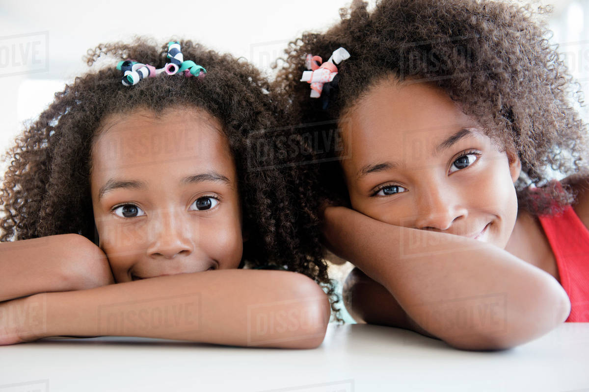 Mixed race sisters leaning on table - Royalty-free Stock Photo | Dissolve