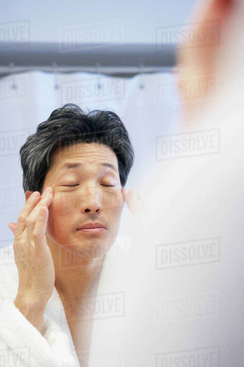 Asian man rubbing face in mirror - Stock Photo - Dissolve