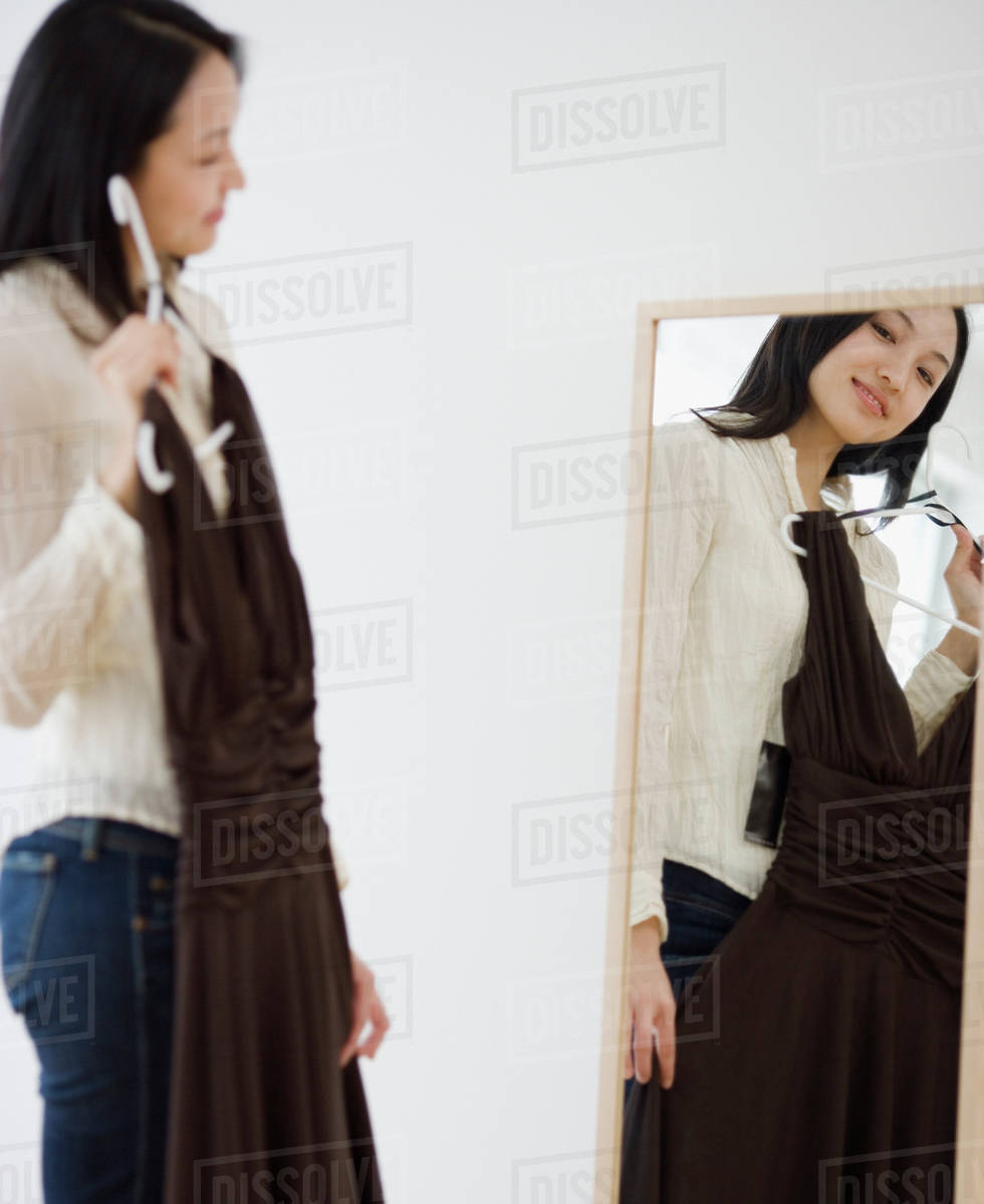 Asian woman holding dress up in front of mirror - Stock Photo - Dissolve