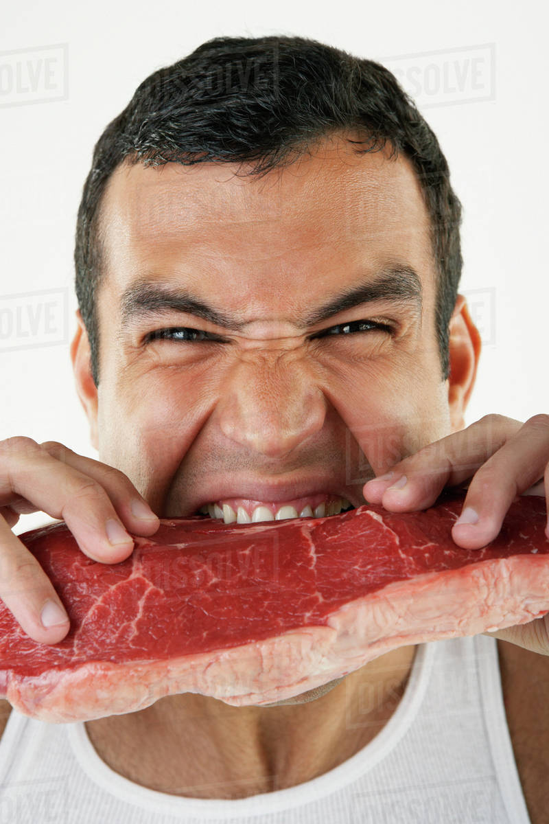 Hispanic man biting raw beef - Stock Photo - Dissolve
