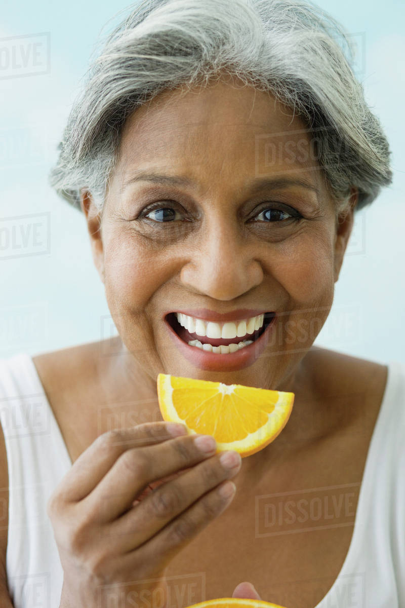 African woman eating orange slice - Stock Photo - Dissolve