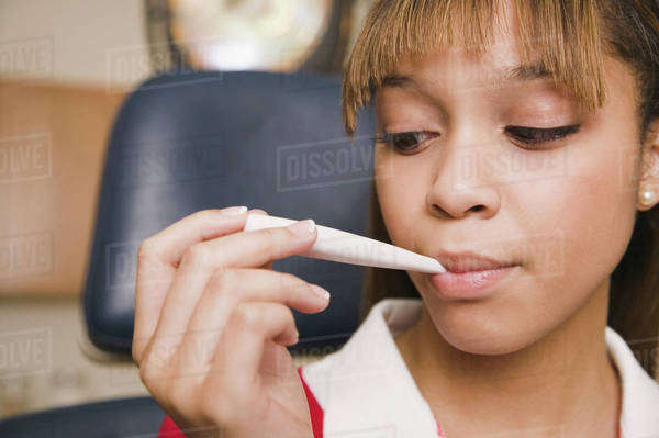 Teenage girl taking temperature with thermometer - Stock Photo - Dissolve