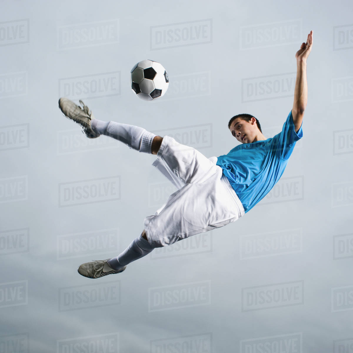 Mixed race teenager in mid-air kicking soccer ball - Royalty-free Stock ...