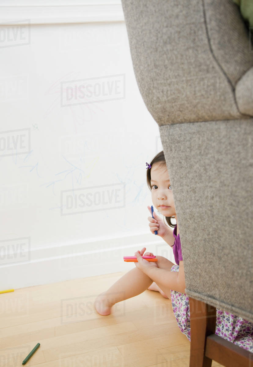 Toddler girl hiding behind chair - Royalty-free Stock Photo | Dissolve