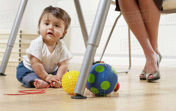 Hispanic baby boy sitting under mother's desk in home office - Royalty ...