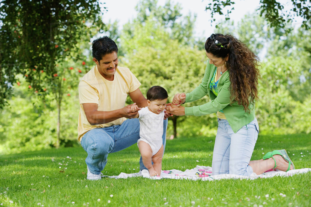 Hispanic parents helping baby walk in park - Royalty-free Stock Photo ...