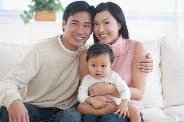 Asian parents holding baby on sofa - Stock Photo - Dissolve