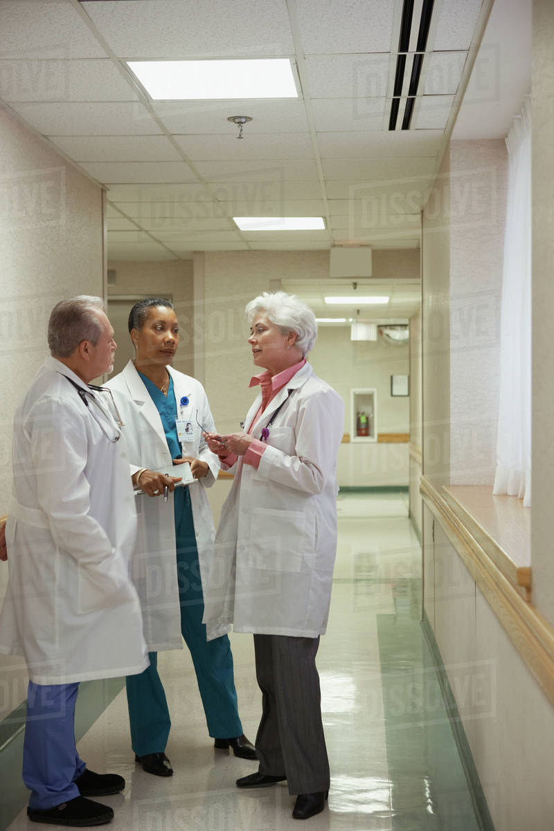 Three doctors talking in hospital hallway - Royalty-free Stock Photo ...