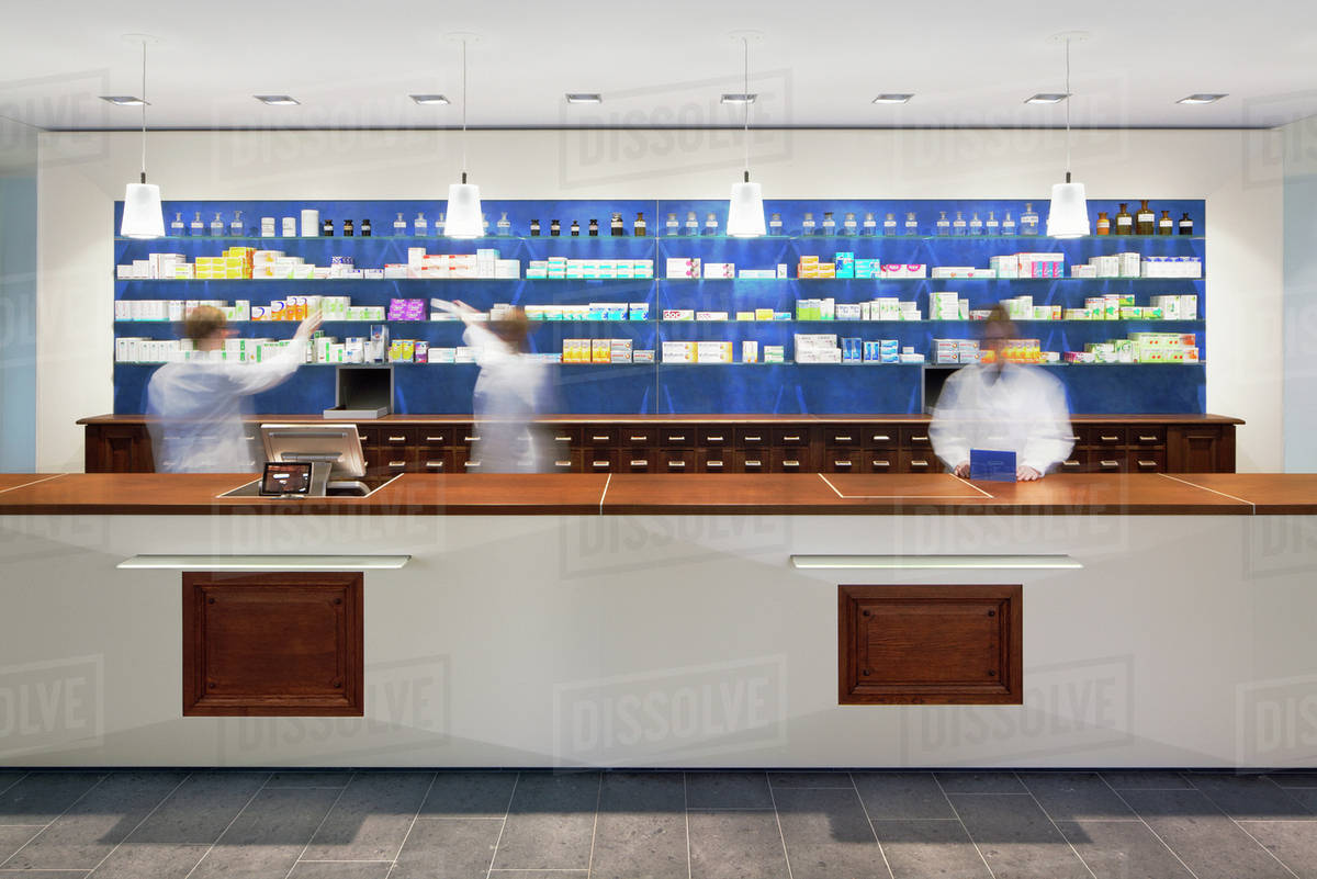 Blurred view of pharmacists behind counter in modern pharmacy - Royalty ...