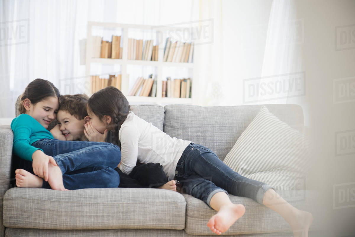 Caucasian brother and sisters whispering on sofa - Royalty-free Stock ...