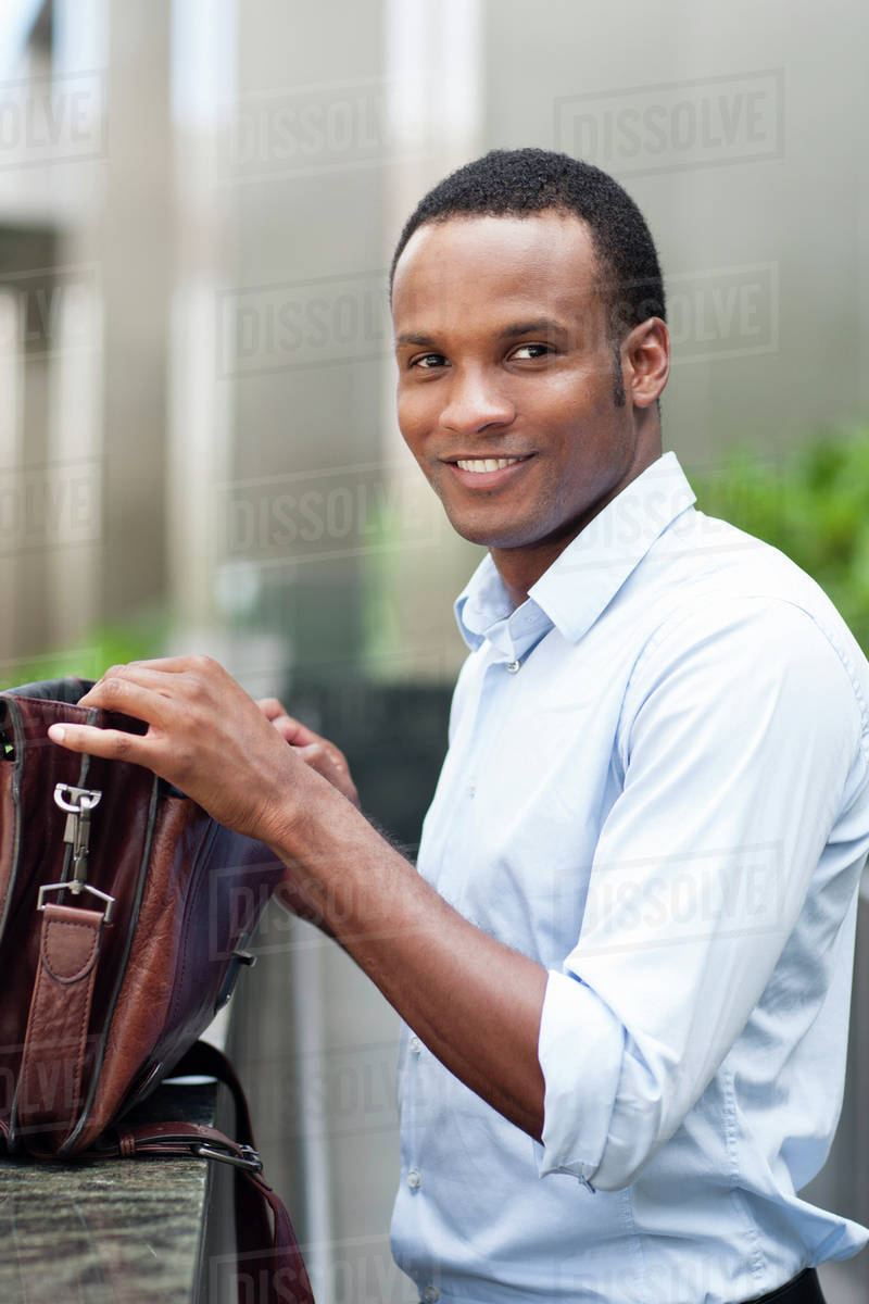 Black businessman opening briefcase outdoors - Stock Photo - Dissolve