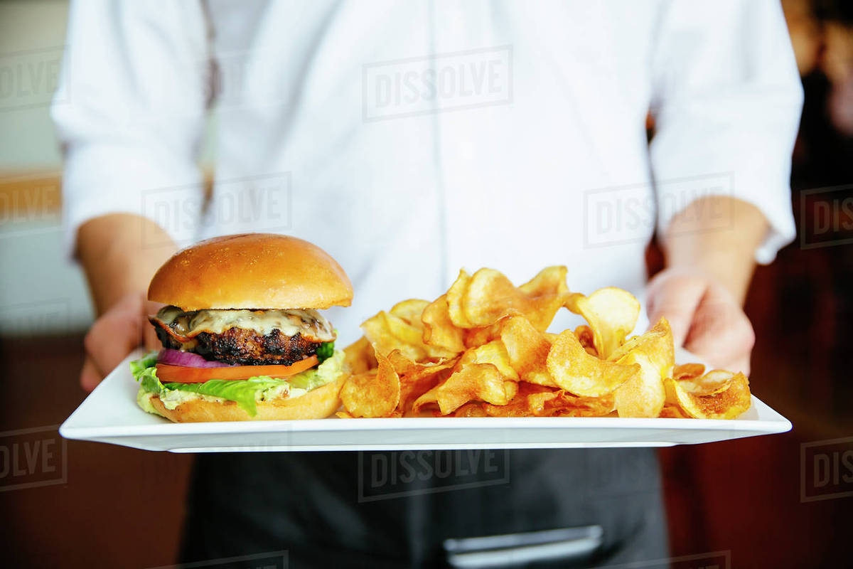 Caucasian waiter holding plate of cheeseburger and chips - Royalty-free ...