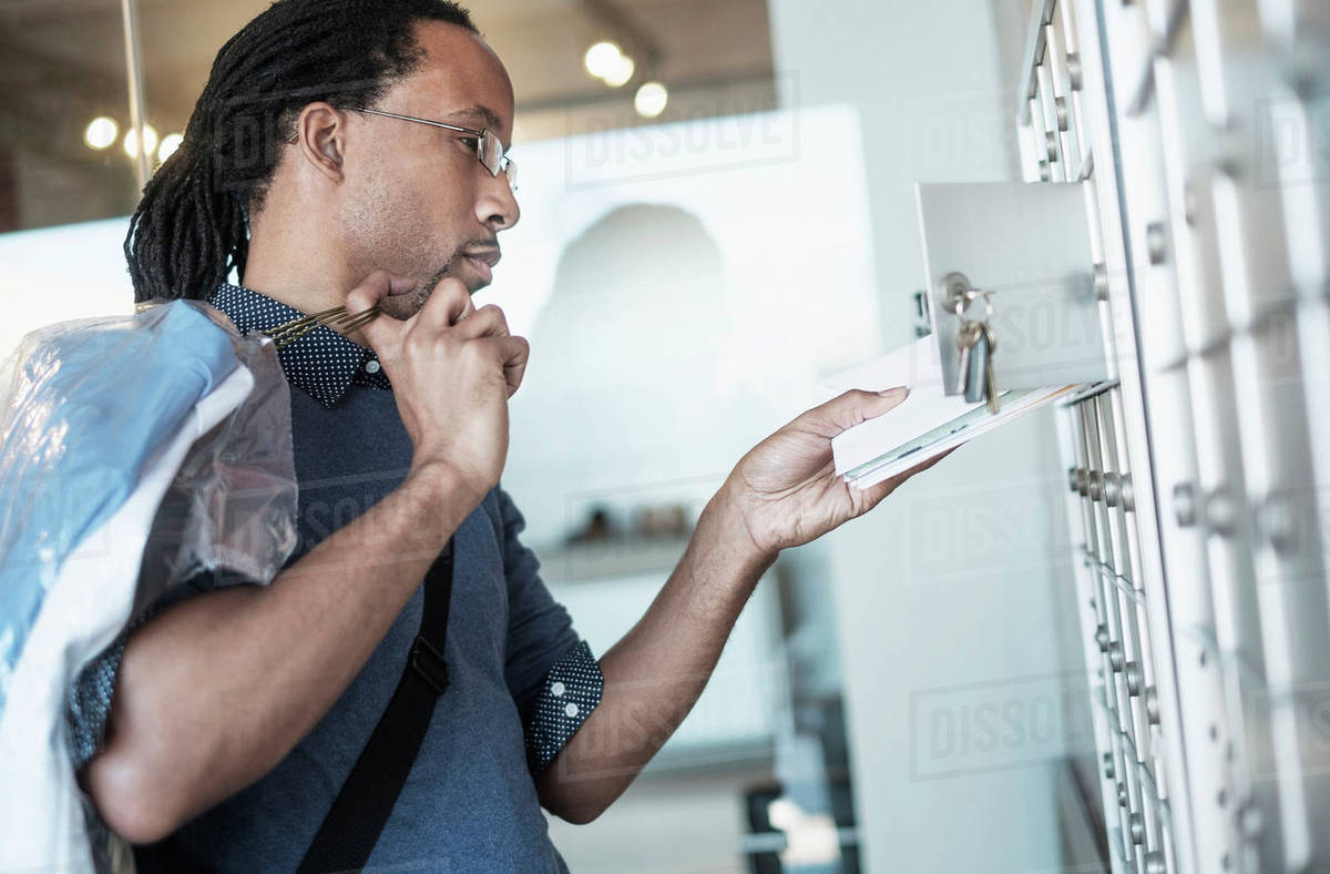 Black man gathering mail from post office box - Stock Photo - Dissolve