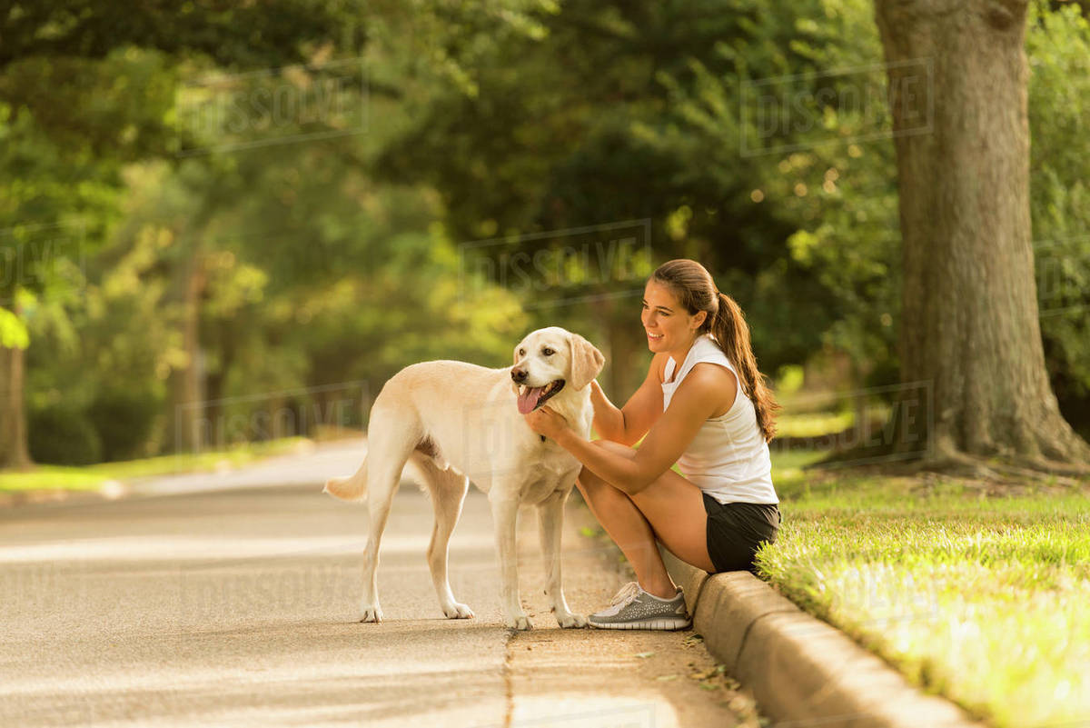 Caucasian woman petting dog on neighborhood street - Stock Photo - Dissolve