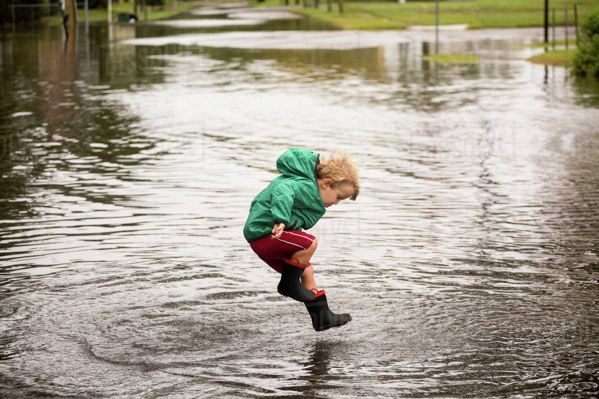 Caucasian boy jumping in puddle - Royalty-free Stock Photo | Dissolve