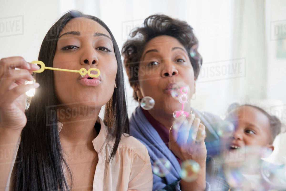 Black multi-generation family blowing bubbles with bubble wand ...