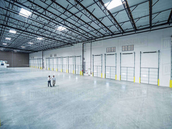 Businessmen walking near loading docks in empty warehouse - Royalty ...