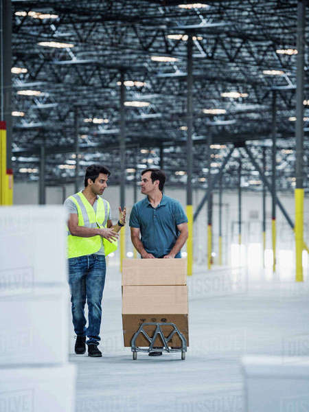 Workers pushing cardboard boxes on hand truck in warehouse - Stock ...