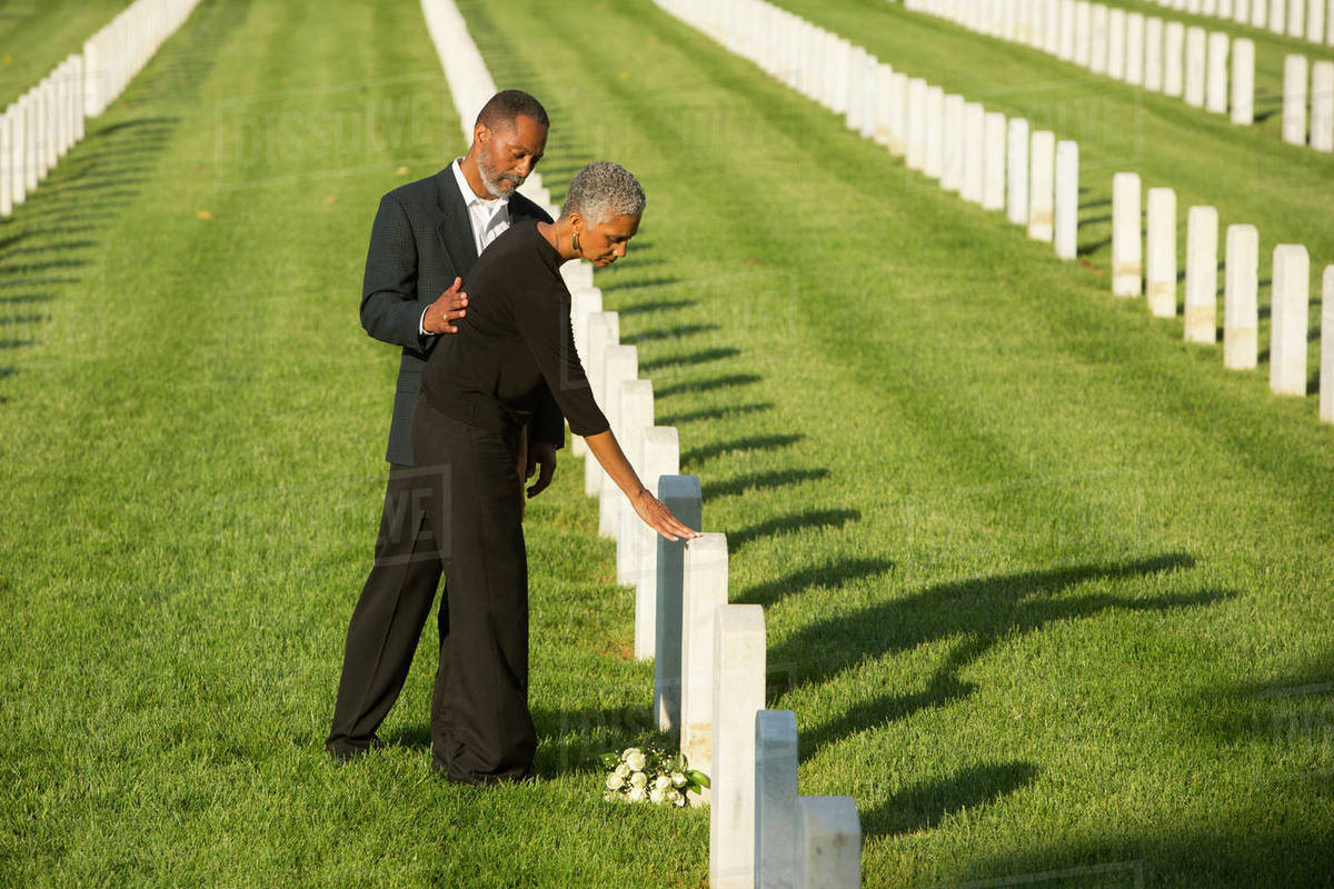 Black couple touching gravestone at military cemetery - Royalty-free ...