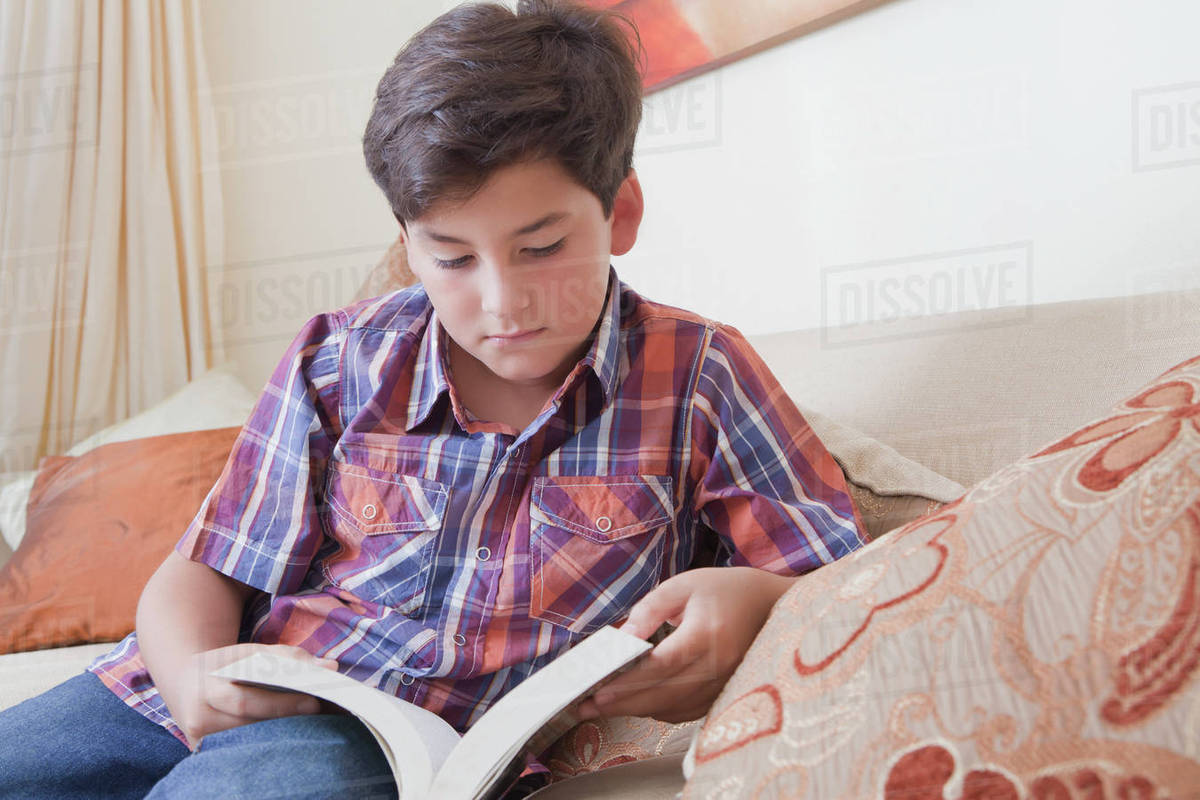 Hispanic boy reading book on sofa - Stock Photo - Dissolve