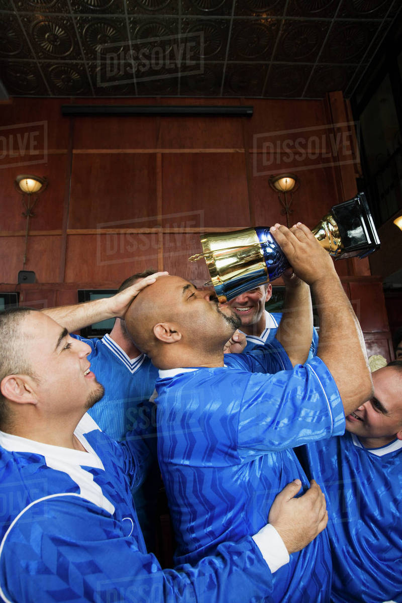 Cheering teammates and man drinking from trophy - Stock Photo - Dissolve
