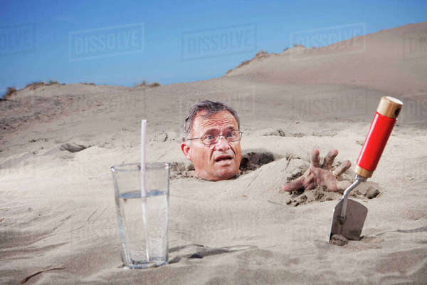 Caucasian man buried in sand next to glass of water and trowel - Stock ...