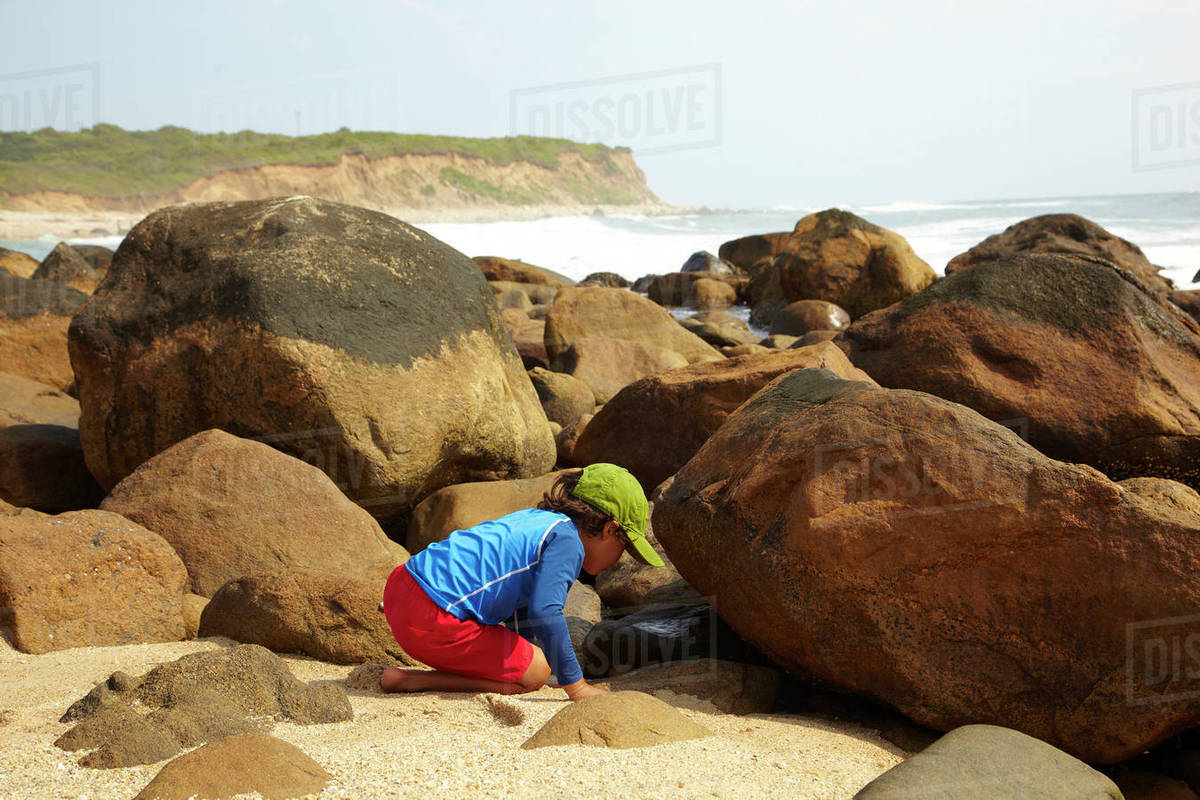 Mixed race boy looking underneath rocks - Stock Photo - Dissolve