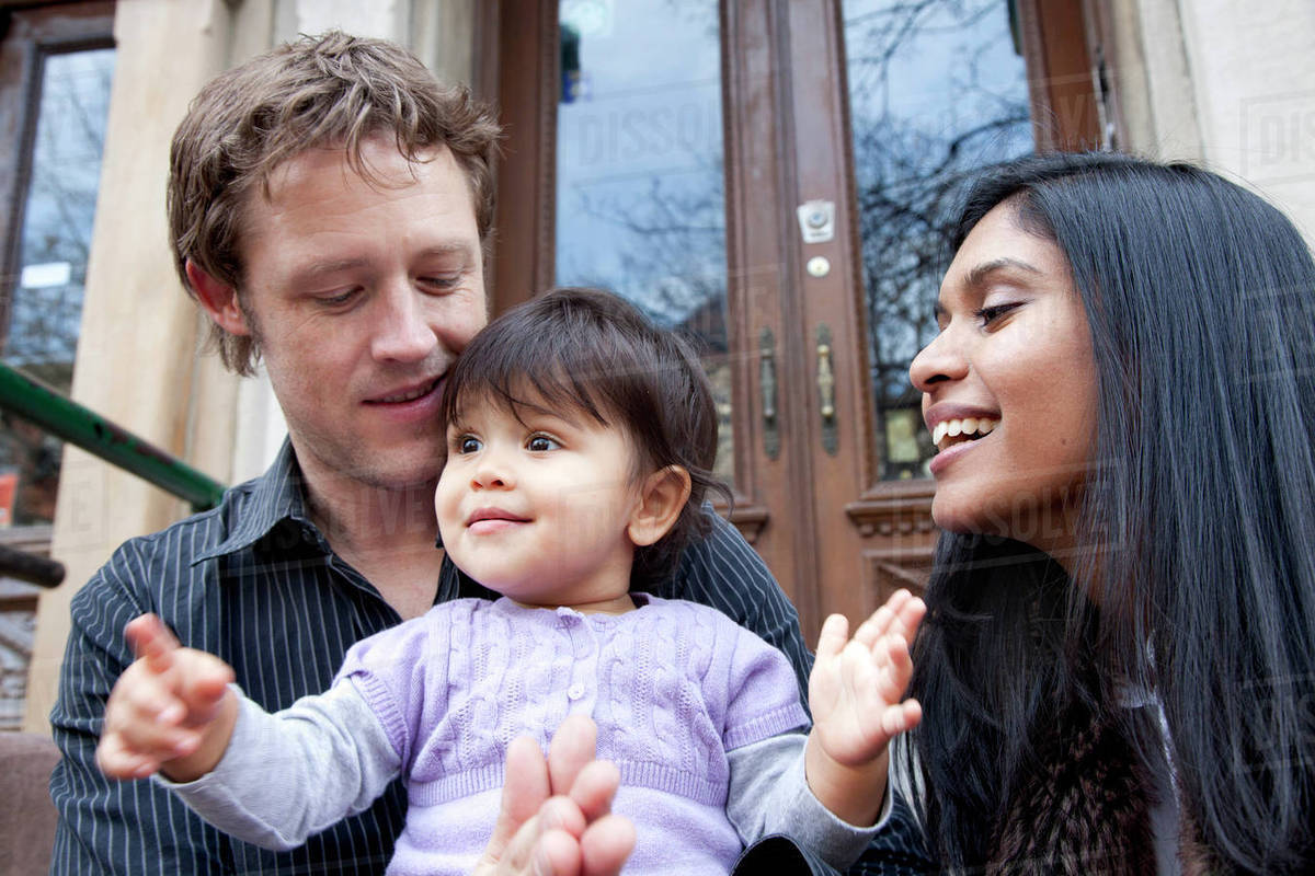 Parent's sitting on front stoop with baby girl - Stock Photo - Dissolve