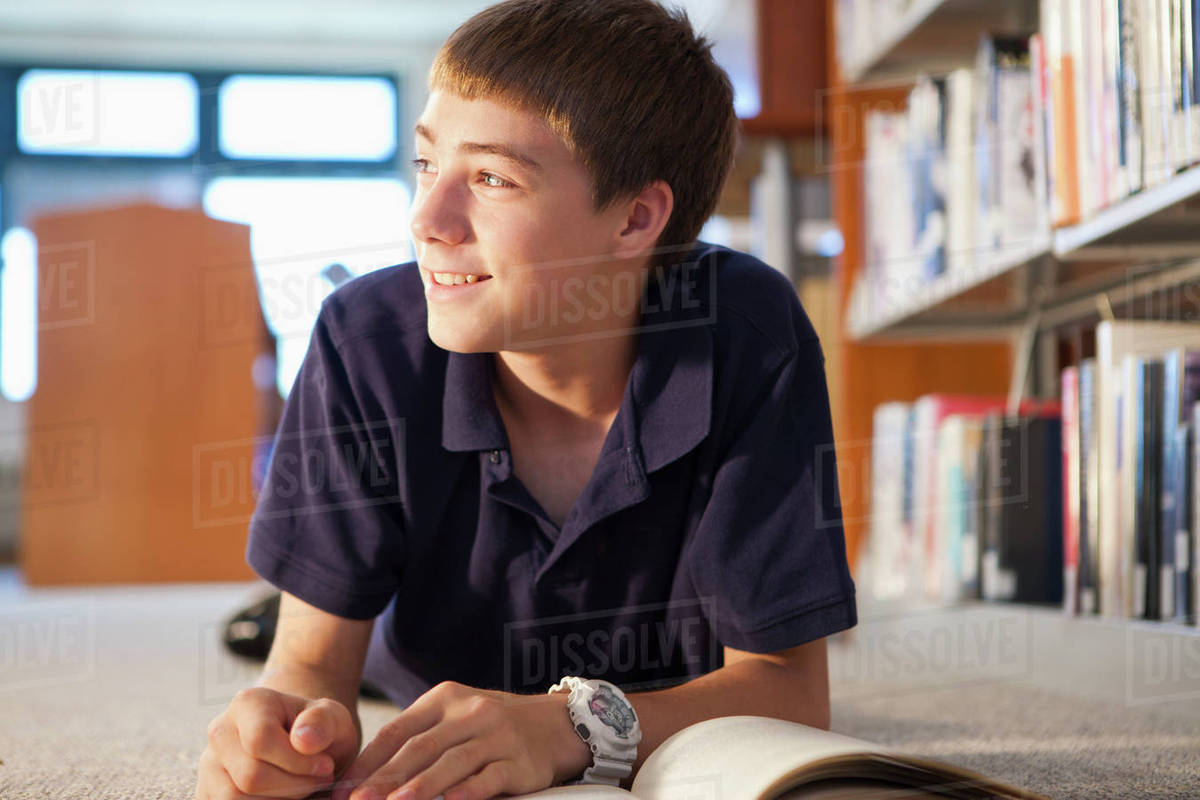 Caucasian boy reading book in library - Royalty-free Stock Photo | Dissolve