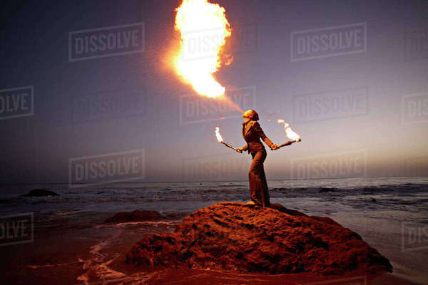 Woman breathing fire on rocky beach - Royalty-free Stock Photo | Dissolve