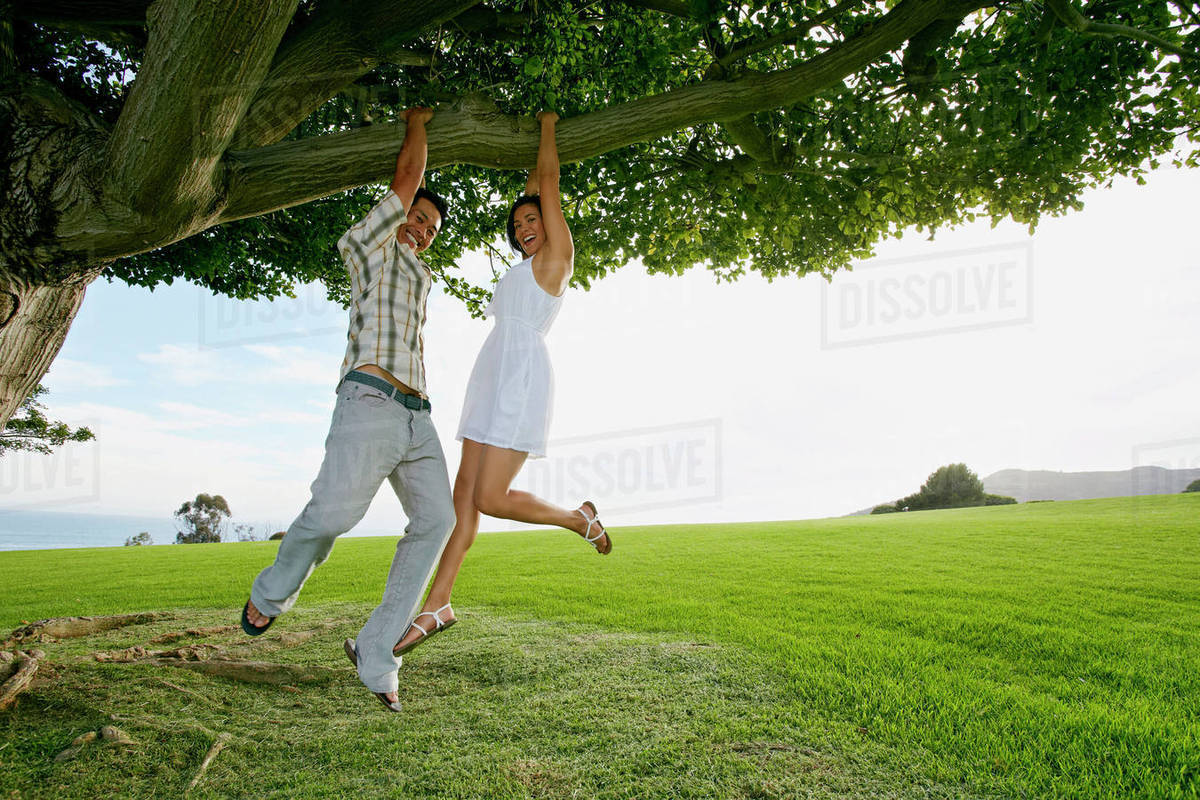 Couple hanging from tree branch in field - Stock Photo - Dissolve