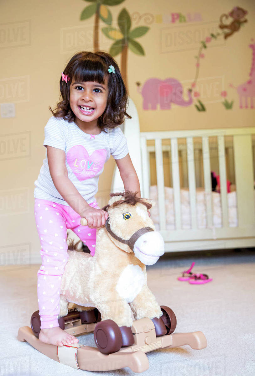 Girl riding rocking horse in nursery - Stock Photo - Dissolve